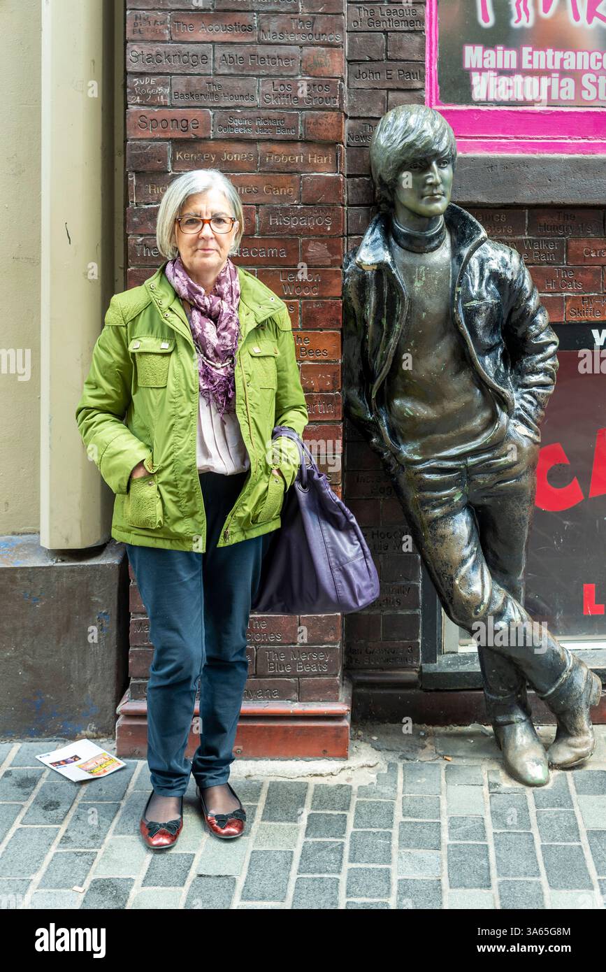 Senior woman standing next to the bronze statue of john lennon in ...