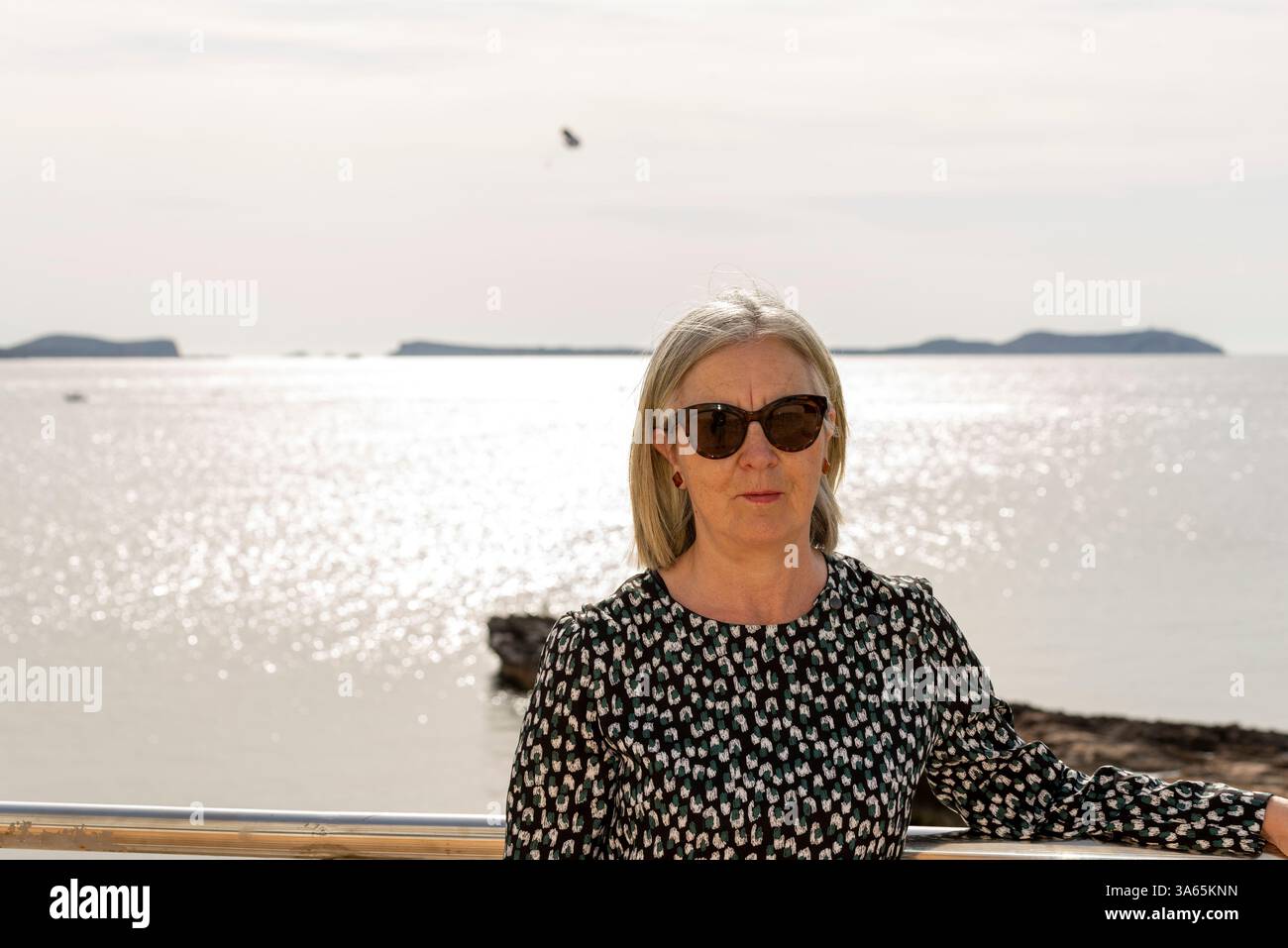 A mature woman stands on a tranquil beach during sunset, reflecting ...