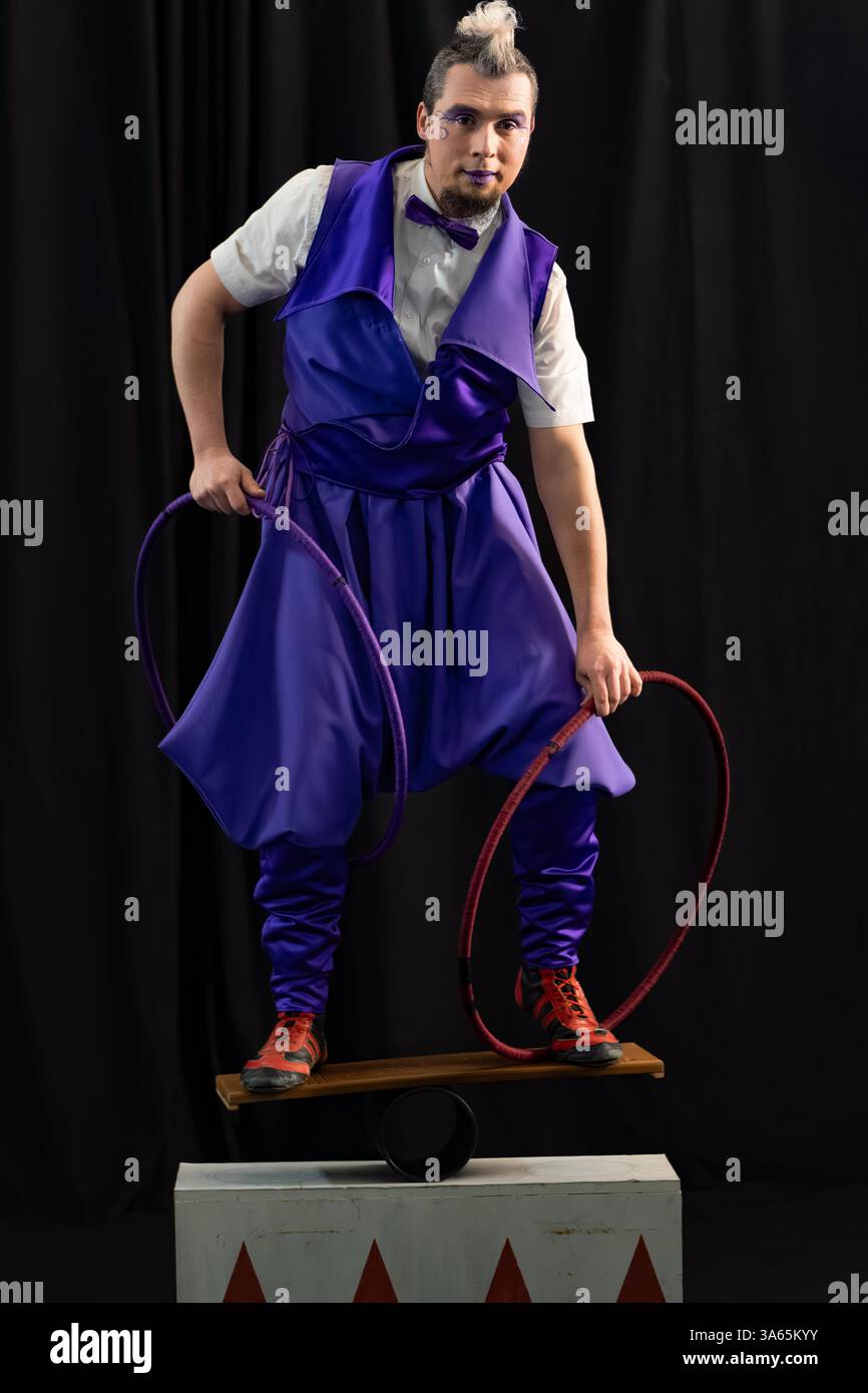 Male artist wearing purple costume balancing on seesaw while holding ...