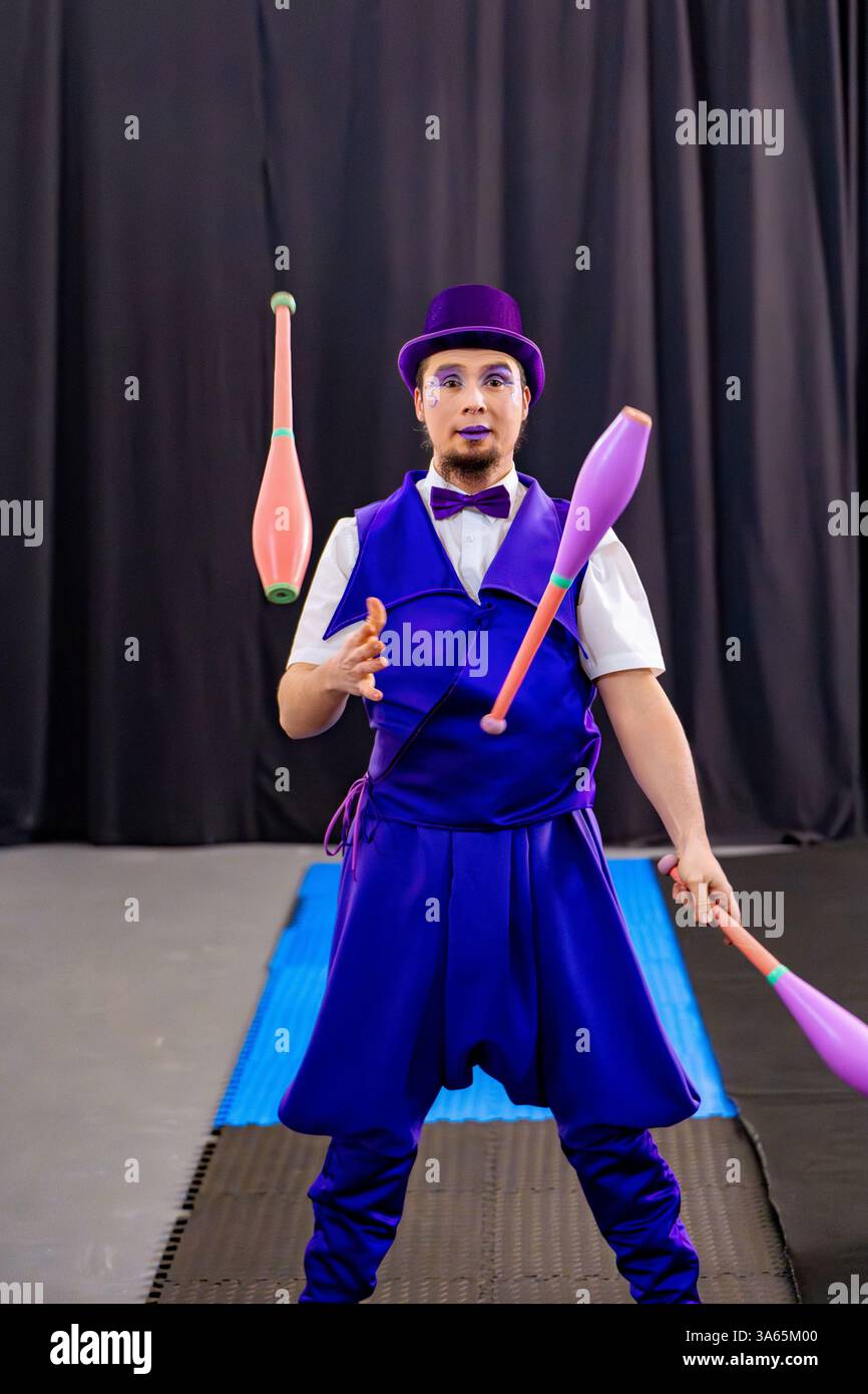 Male artist juggling colorful clubs while wearing a vibrant purple ...