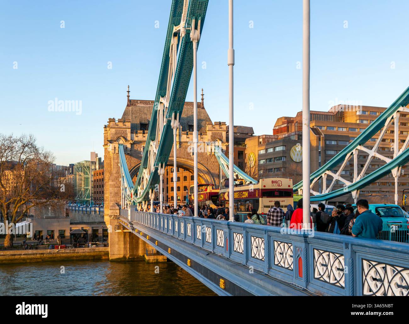 People and open top tour buses cross Tower Bridge in late afternoon ...