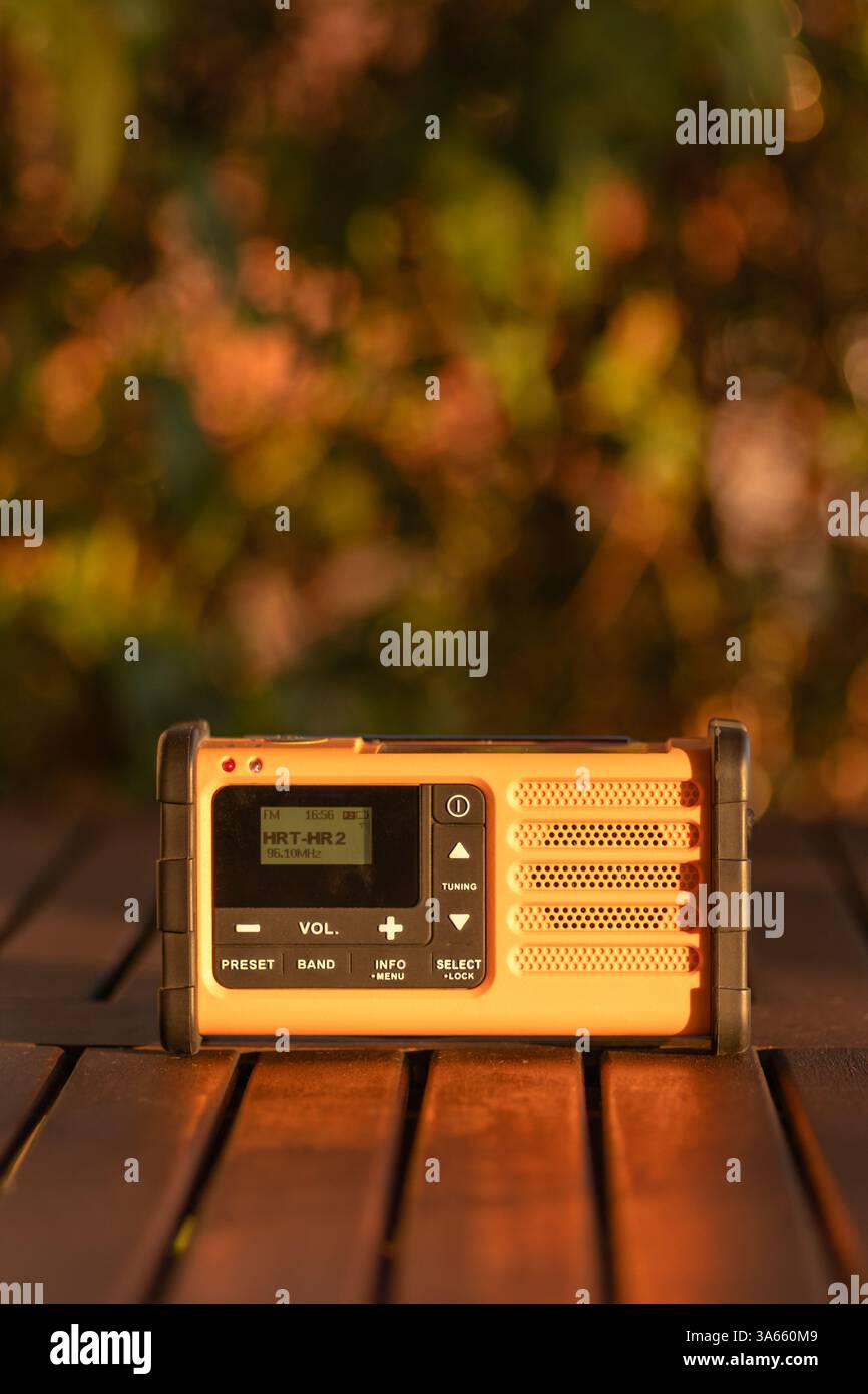 A compact orange portable radio device sits on a wooden table lit by ...