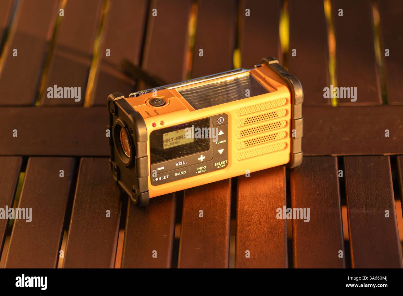 A compact orange portable radio device sits on a wooden table lit by ...
