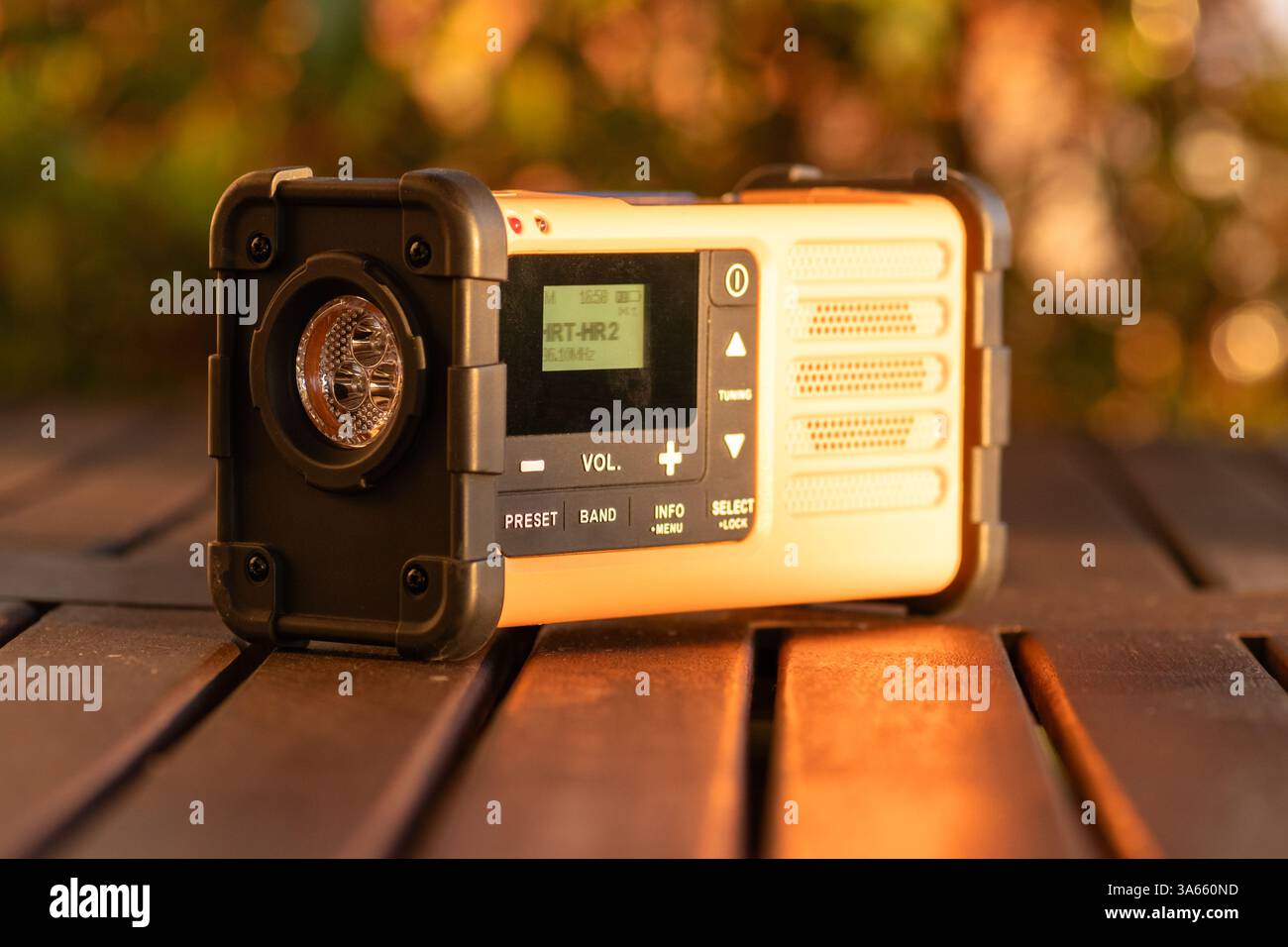 A compact orange portable radio device sits on a wooden table lit by ...