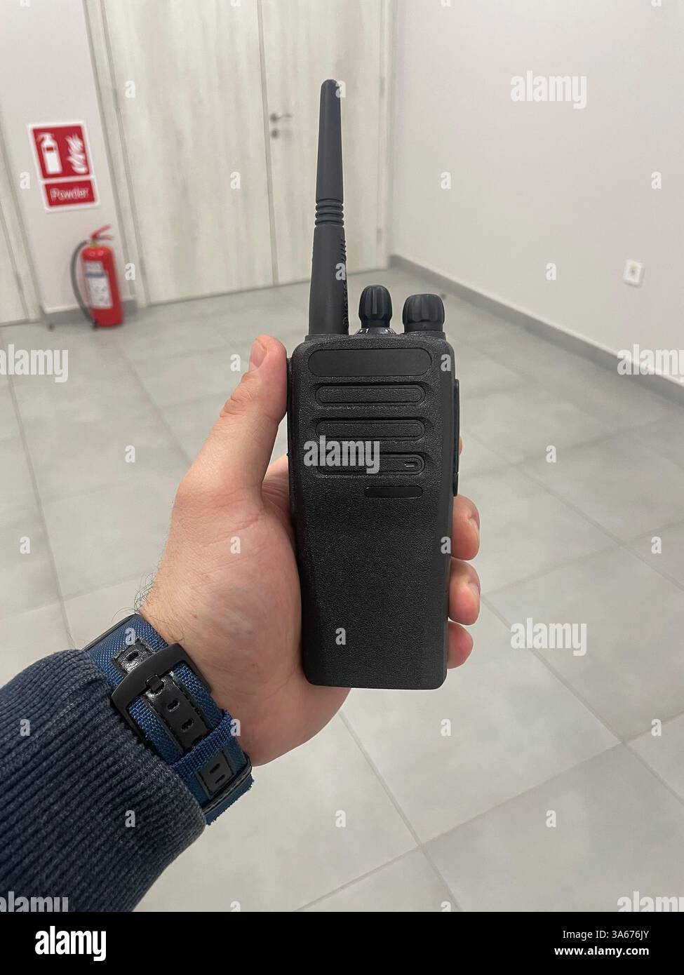 A hand holding a black walkie-talkie with an antenna indoors Stock ...