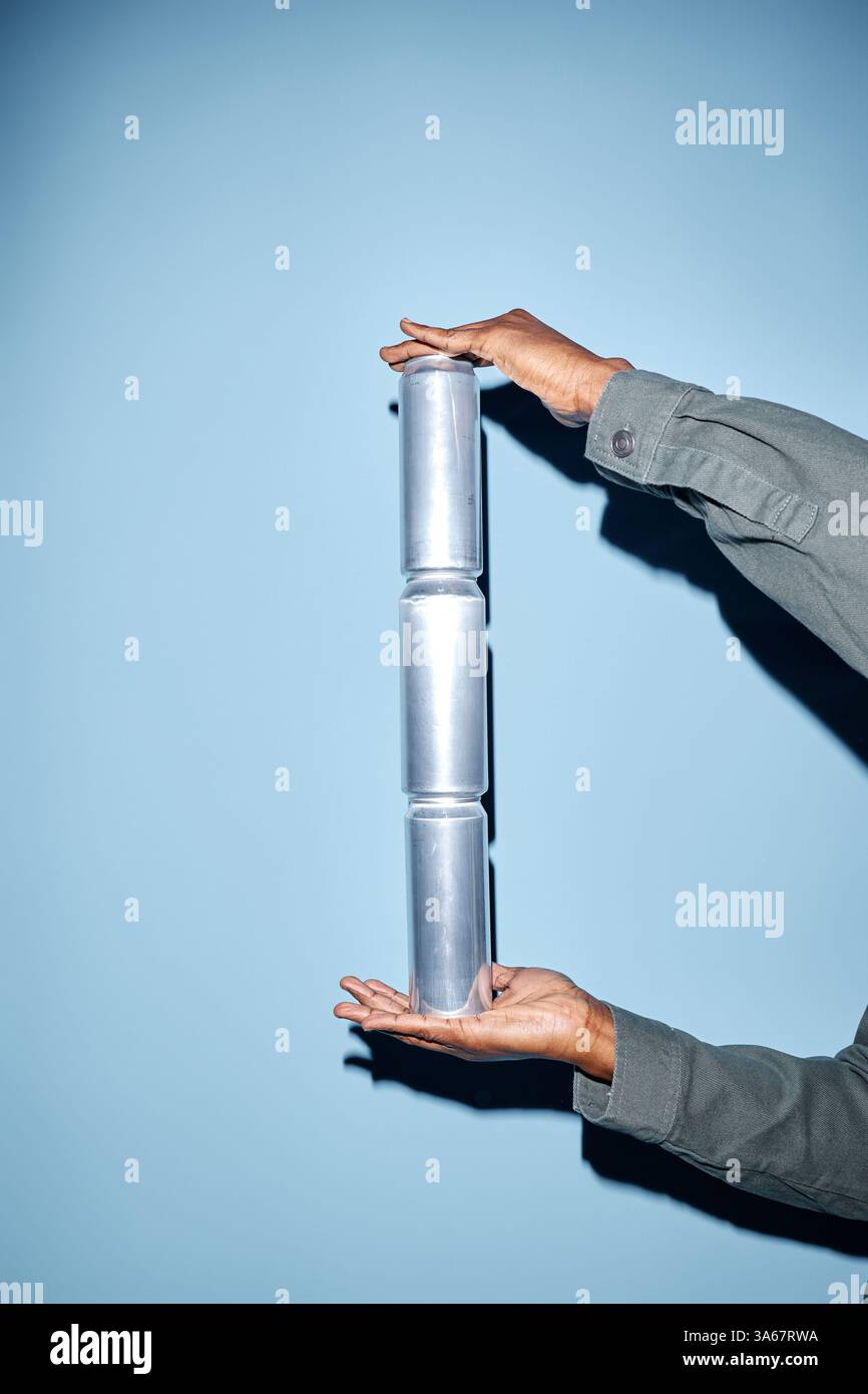 Hand holding stack of stainless steel coffee cups against a blue ...