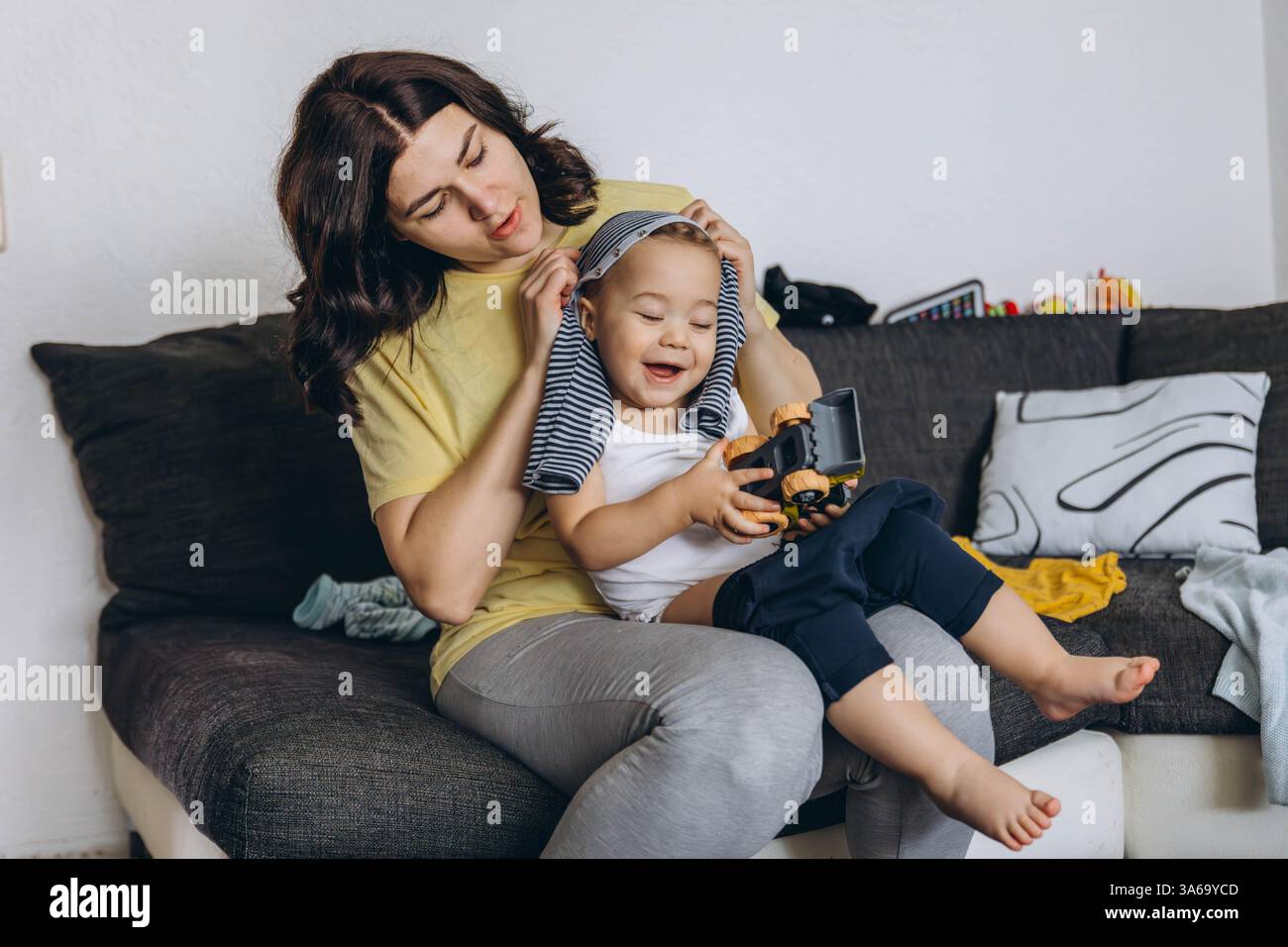 Mother changing her baby, while the baby laughs, holding a toy car in ...