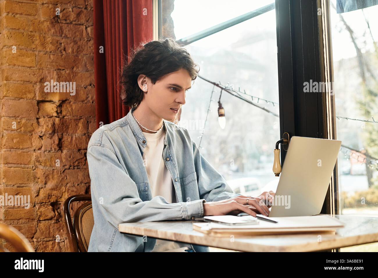 A young man works at a cozy cafe, relaxed and enjoying the warm natural ...