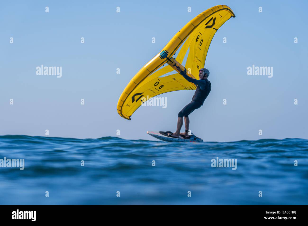 A man wingfoils at sea using a hand held inflatable wing, riding a ...