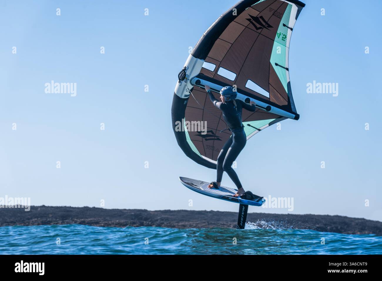 A young woman wingfoils at sea using a hand held inflatable wing ...