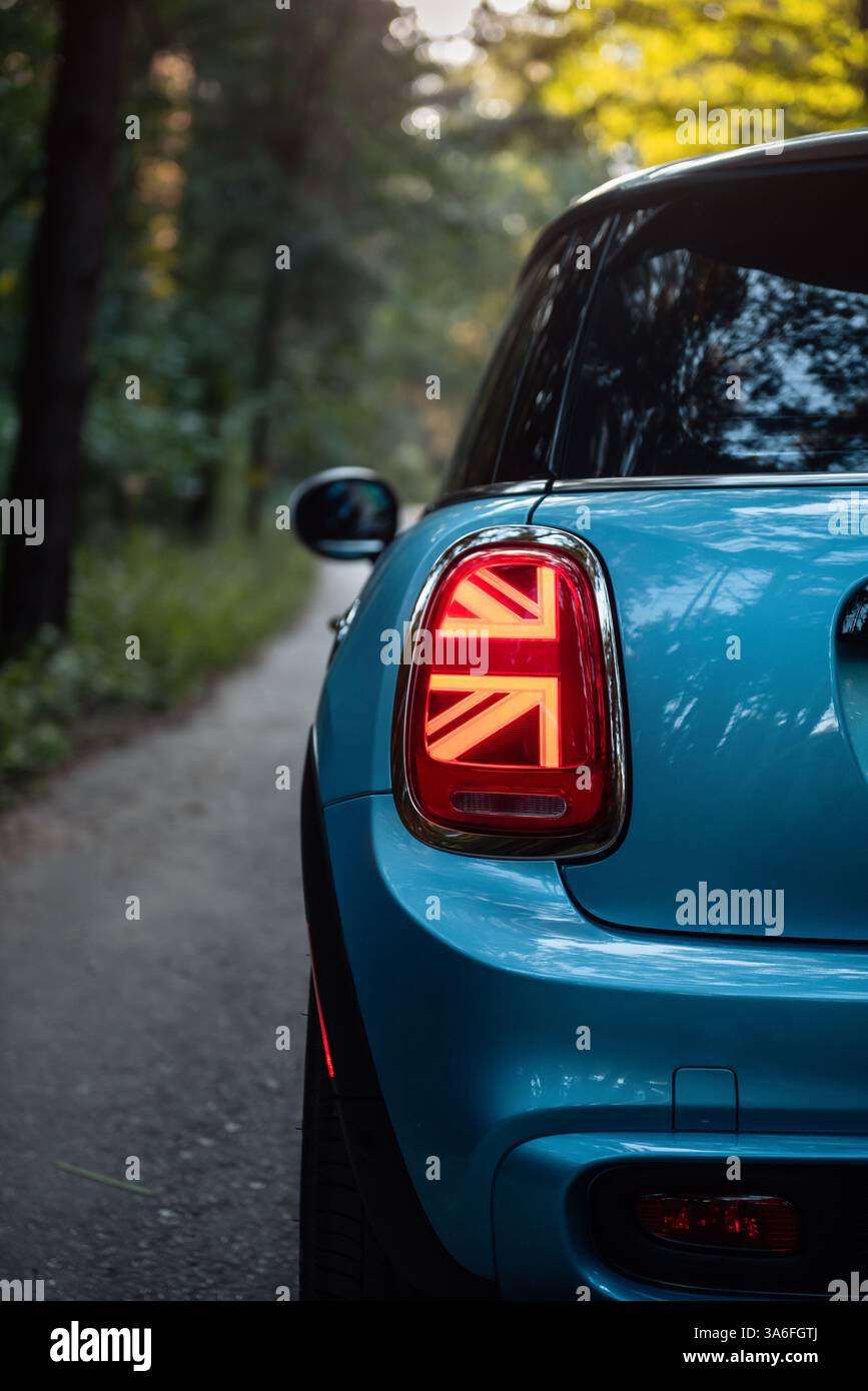 Blue Mini Cooper on a forest road in late afternoon. Rear view of ...