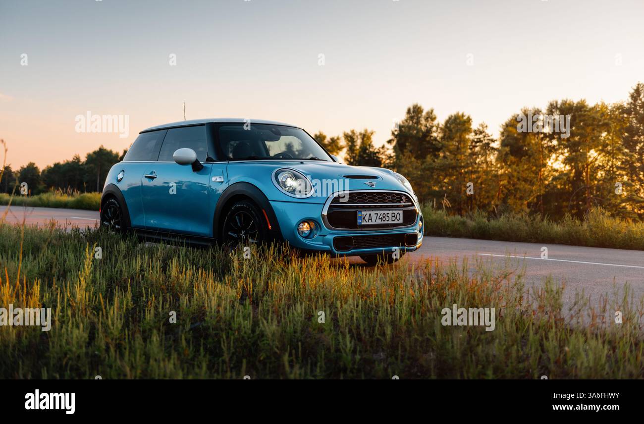 Blue Mini Cooper on countryside road at sunset. Three quarter front ...