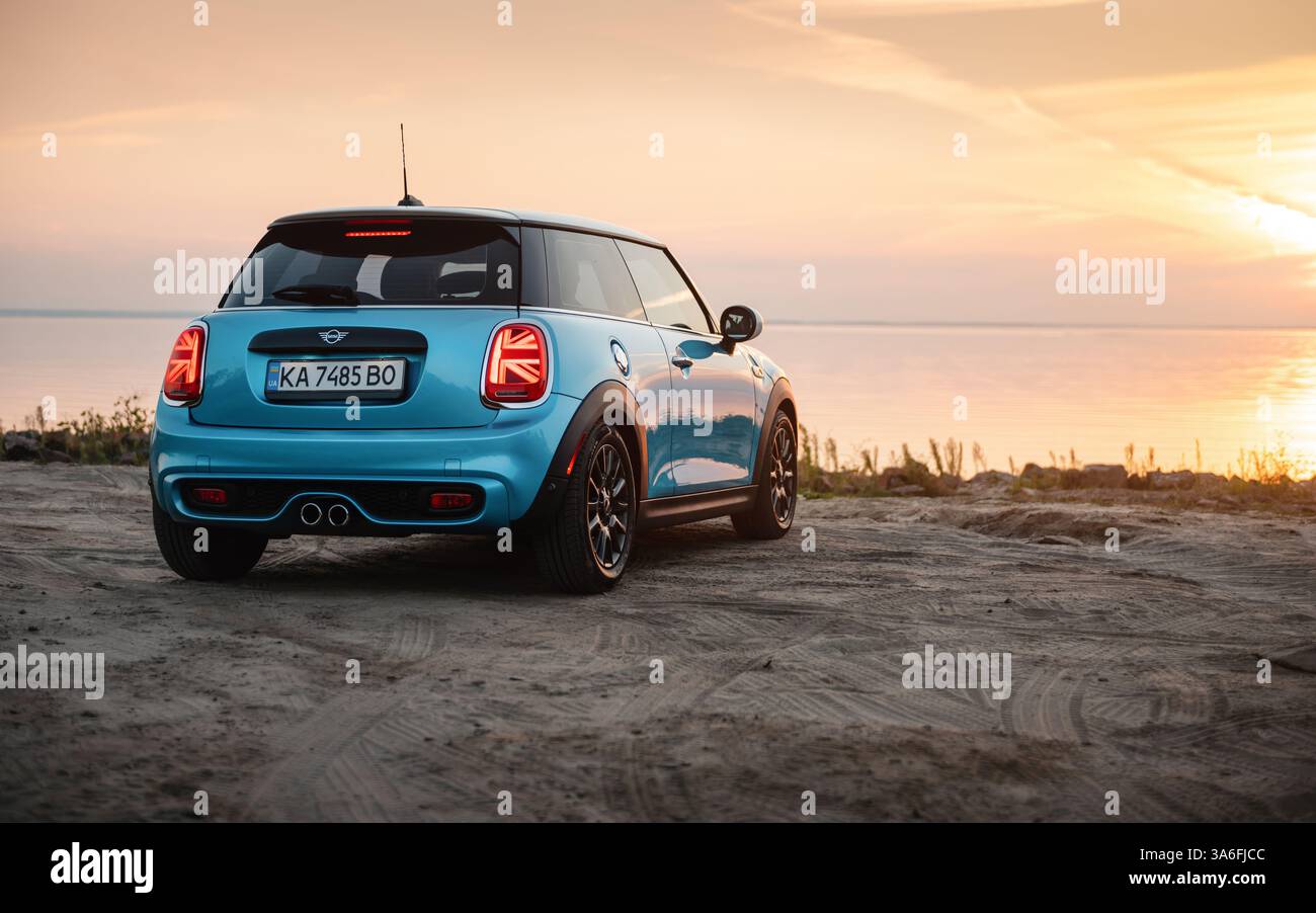 Blue Mini Cooper on a beach at sunset. Three quarter rear view of ...