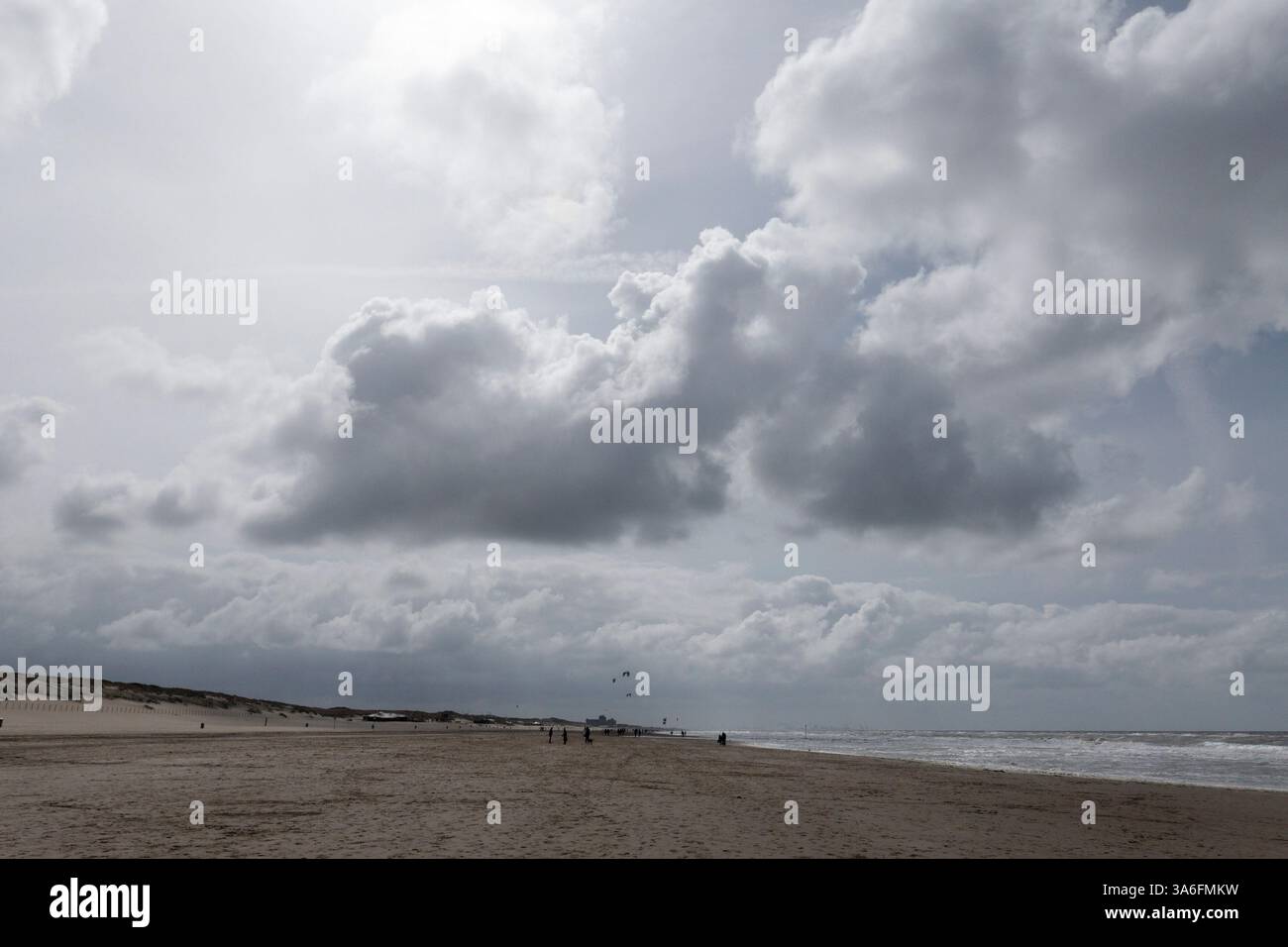 Sky with dramatic clouds with a wide, almost emtpy beach and dunes ...