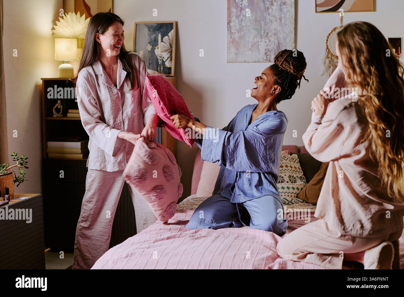 Three best friends holding pink cushions and laughing loudly while ...