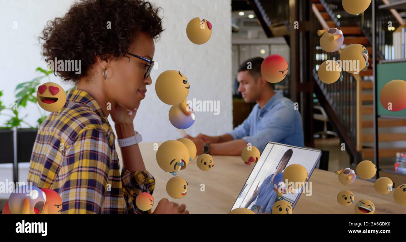 African American woman using laptop with floating emojis in modern office. Diversity, technology ...