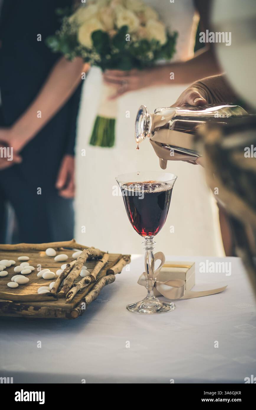 The priest fills a glass with red wine, during a greek orthodox wedding ...
