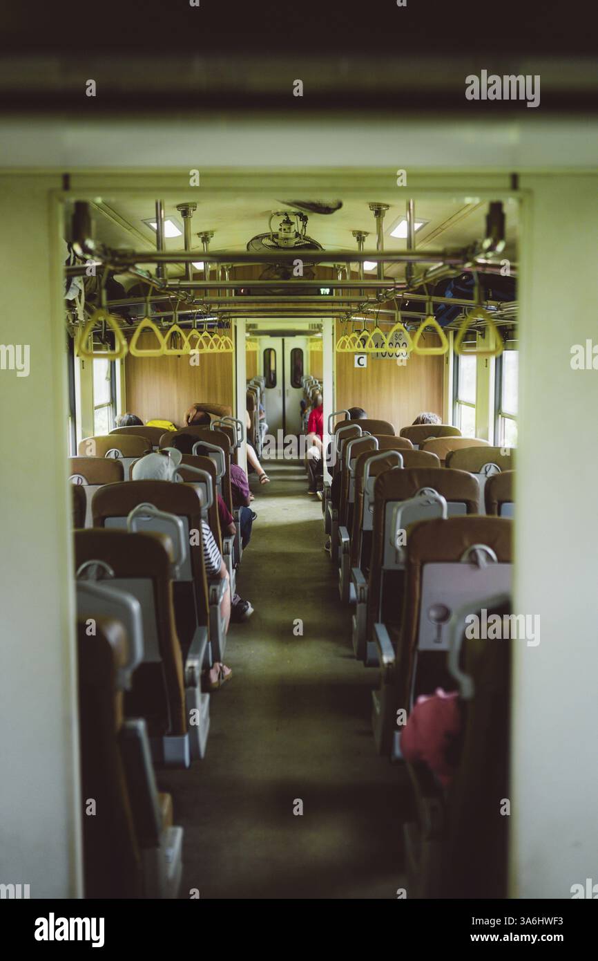 Interior view of a train compartment with seated passengers in subdued ...