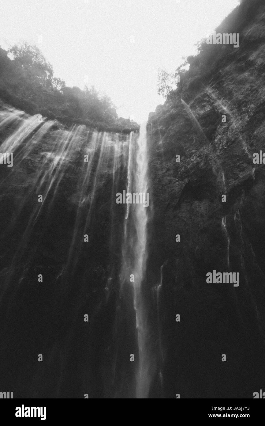 A high waterfall flows between steep rocks in a black and white nature ...