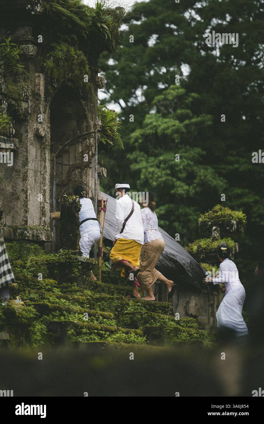People in traditional dress enter a moss-covered temple complex together, Munduk, Sri Lanka ...