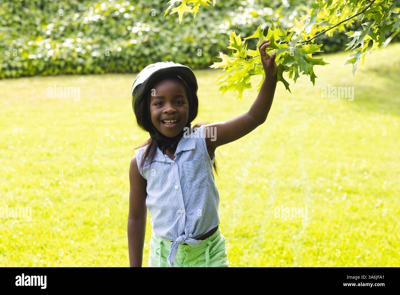 African American girl wearing helmet smiling and touching tree branch ...