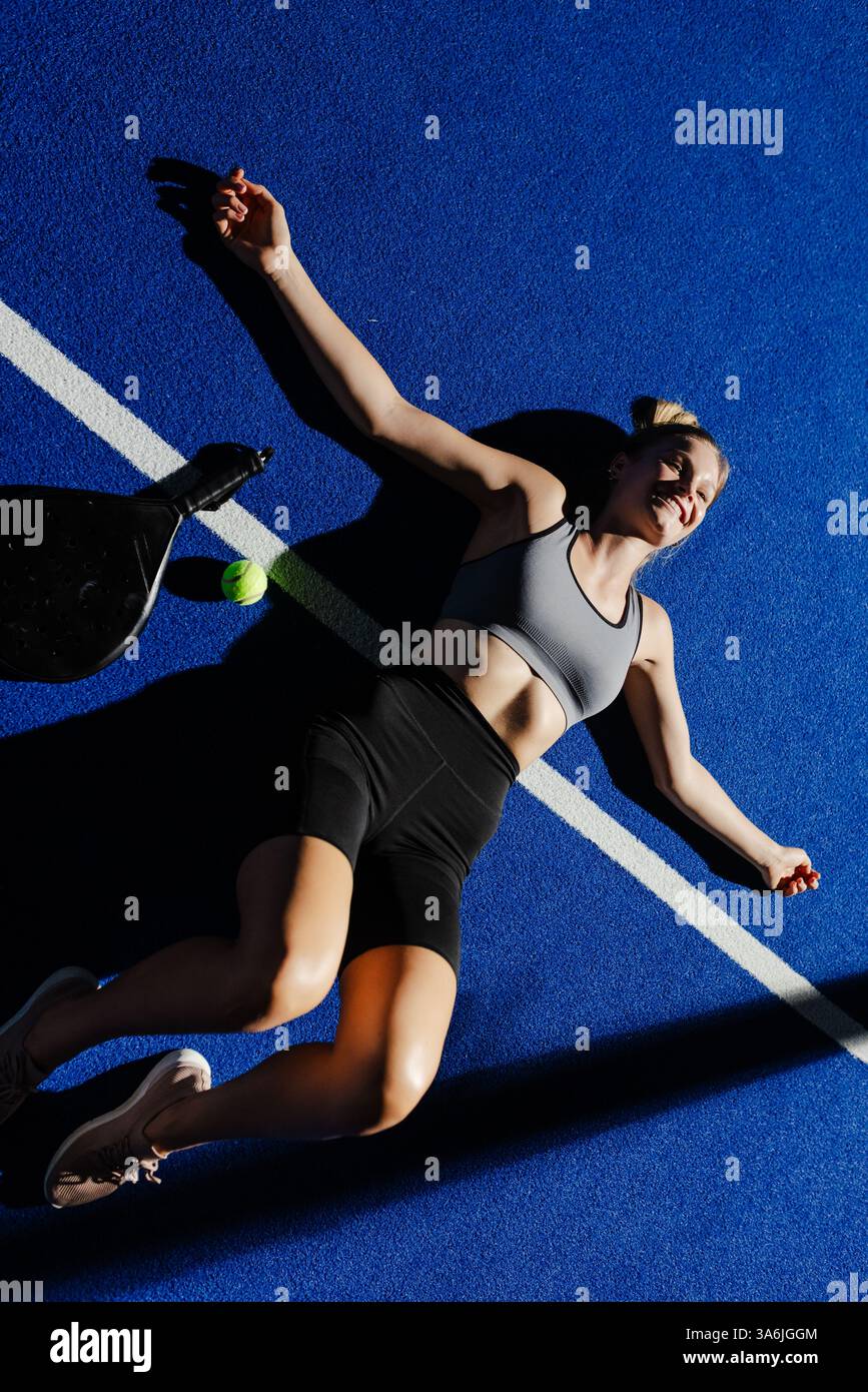 Exhausted woman resting on court after padel tennis match, smiling ...