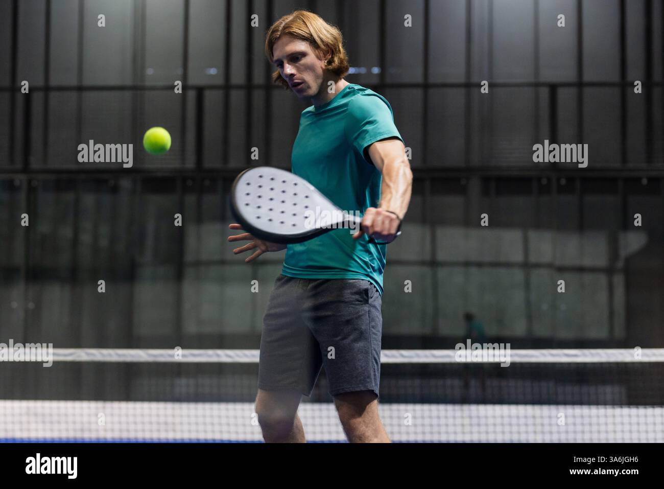 Focused man playing padel tennis, hitting ball with racket on court ...