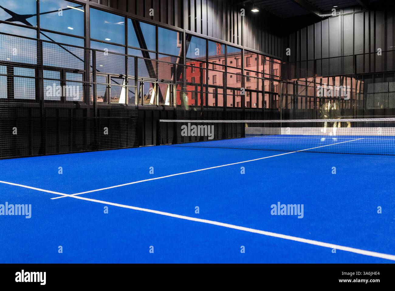 Empty indoor padel tennis court with blue flooring and glass walls ...
