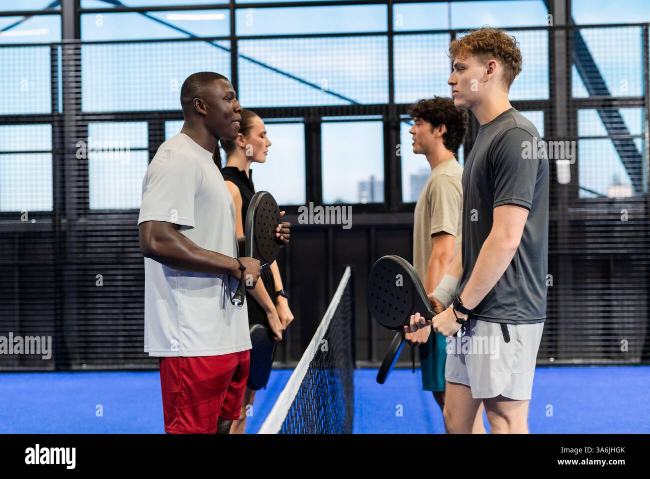 Players holding paddles facing each other on indoor padel tennis court ...