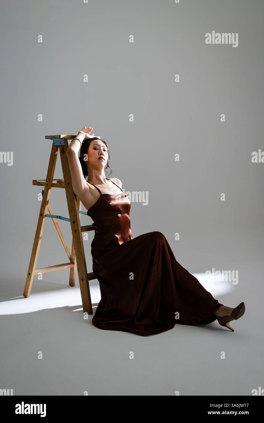 Elegant asian woman in brown dress posing gracefully next to wooden ...