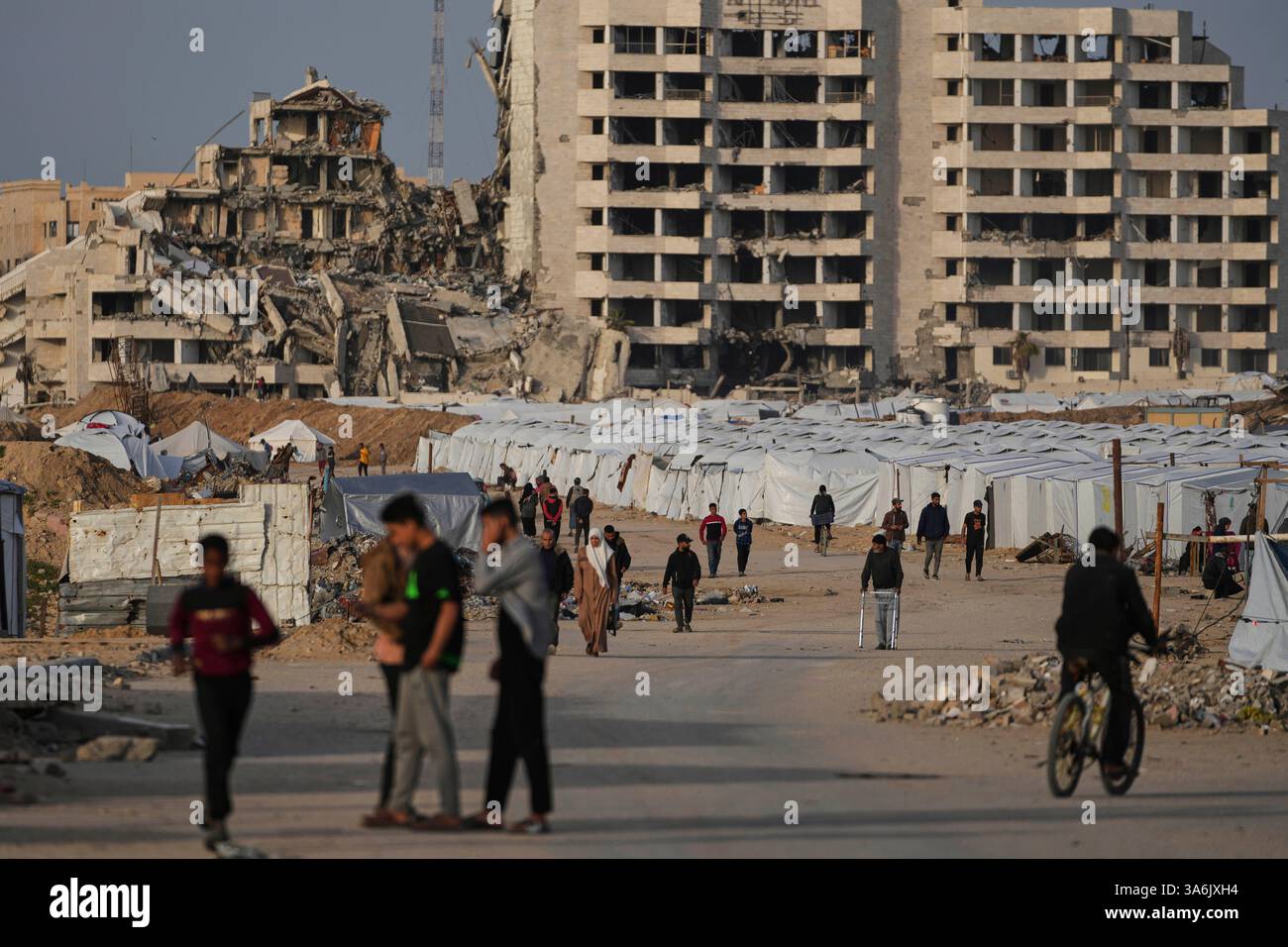 Palestinians walk next to a tent camp for displaced by the Israeli air ...