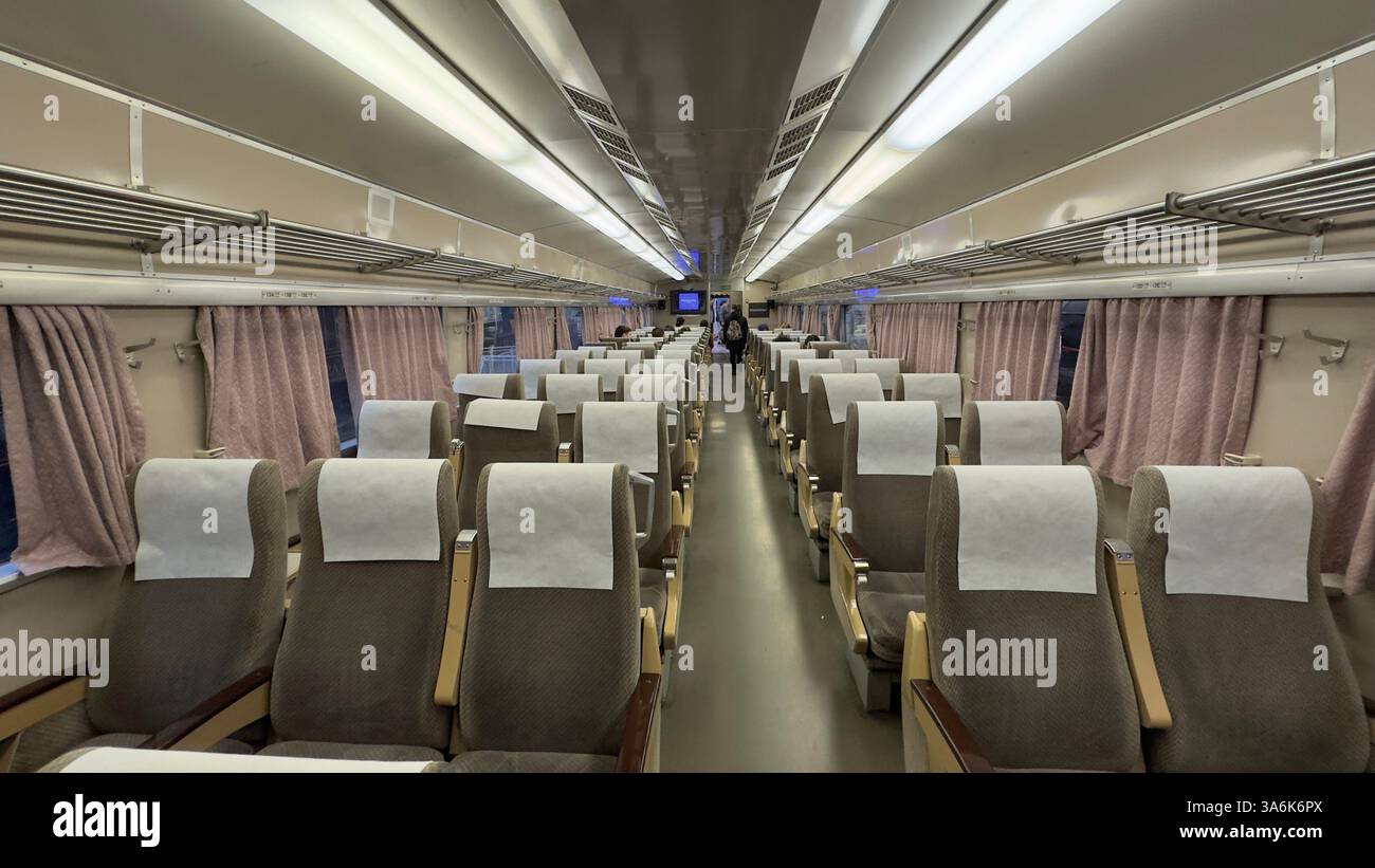 Interior shot of an empty train car, showing rows of seats and an aisle. Neutral color palette ...