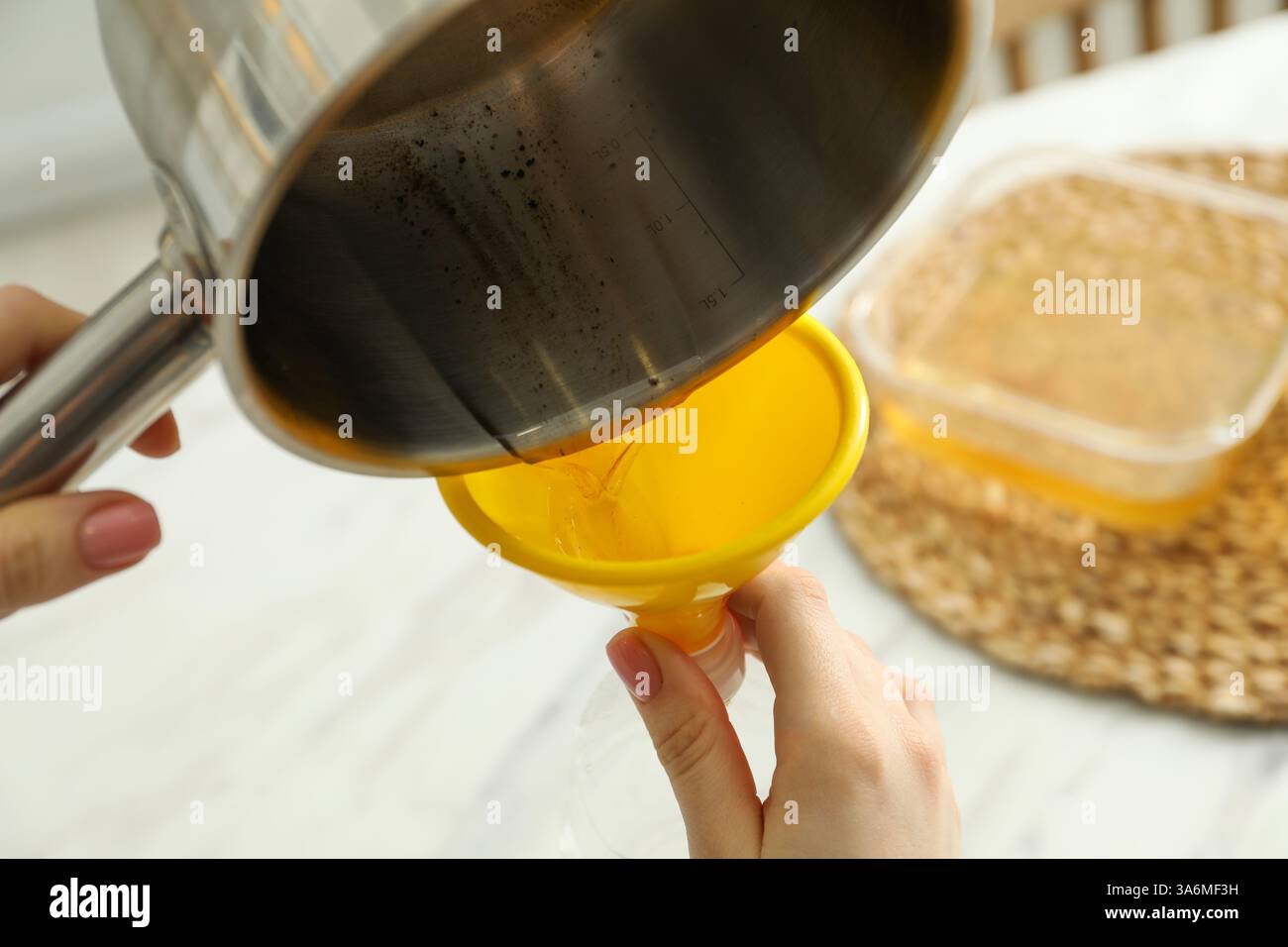 Woman pouring used cooking oil into bottle through funnel in kitchen ...