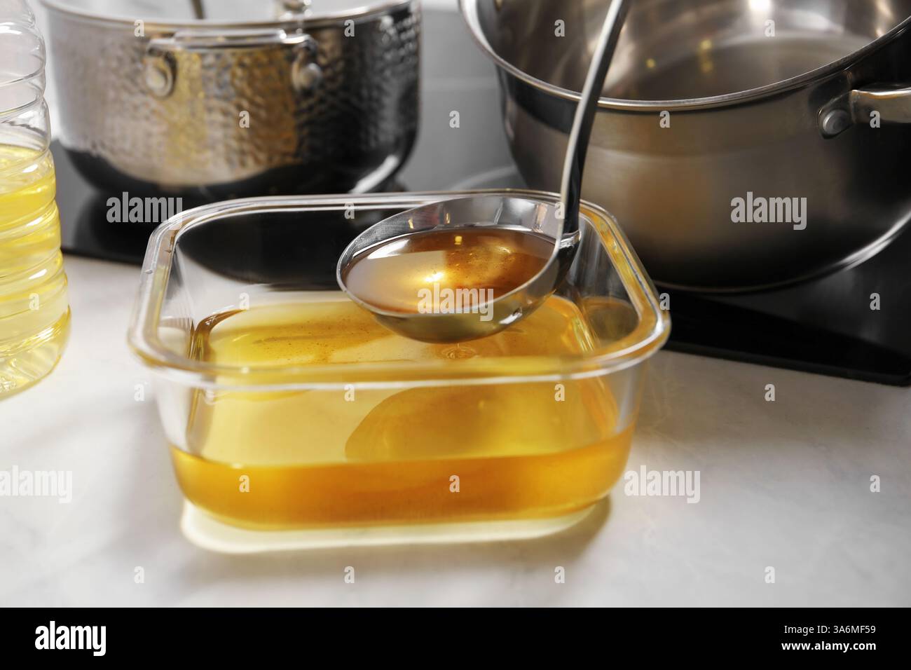 Pouring used cooking oil into glass container at white countertop ...