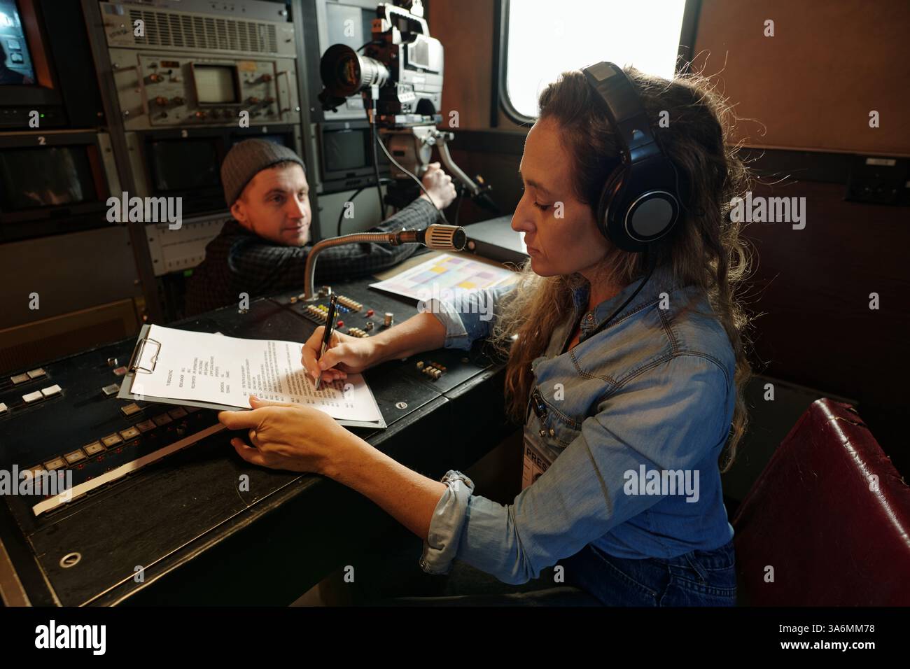 Modern female journalist in headphones sitting by workplace with ...