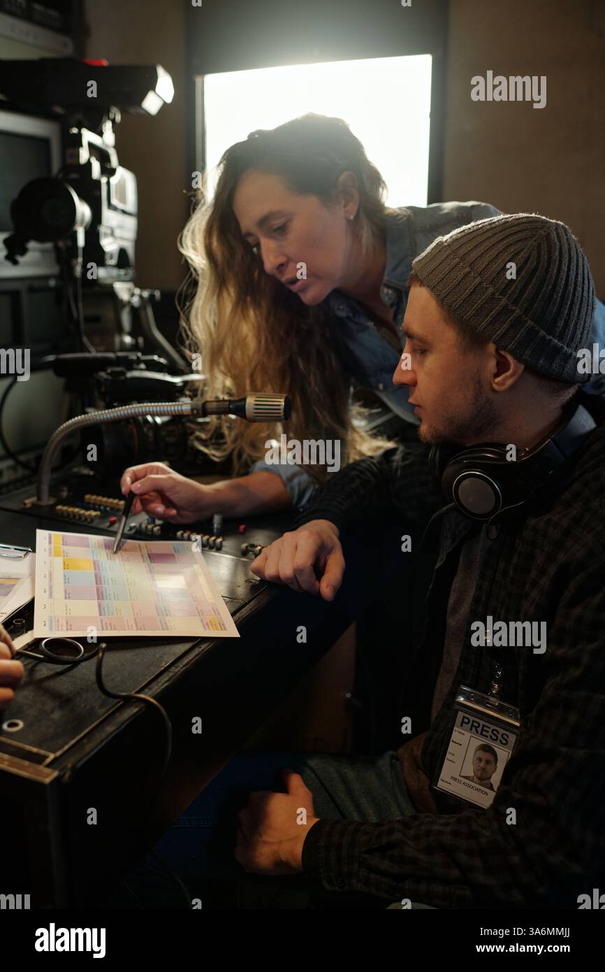 Young female journalist pointing at broadcast schedule while discussing ...