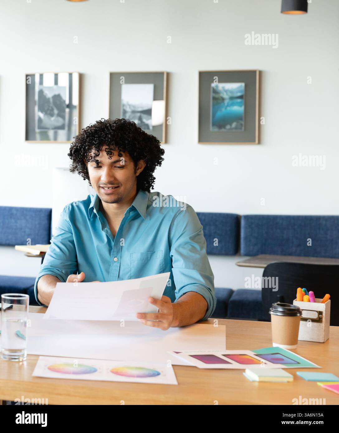 Smiling man reviewing documents at office desk with coffee and colorful ...