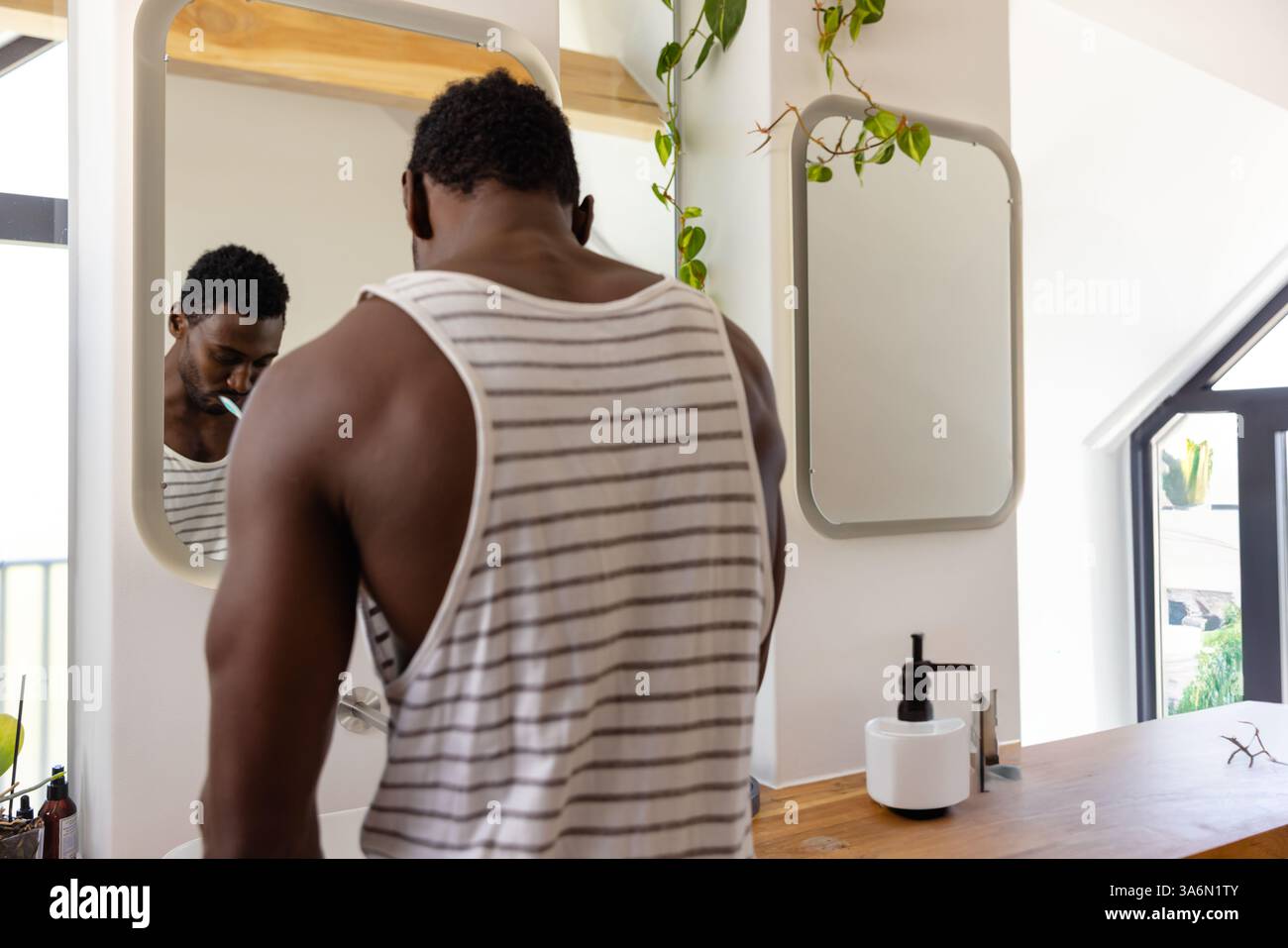 Man brushing teeth in modern bathroom, wearing striped tank top ...