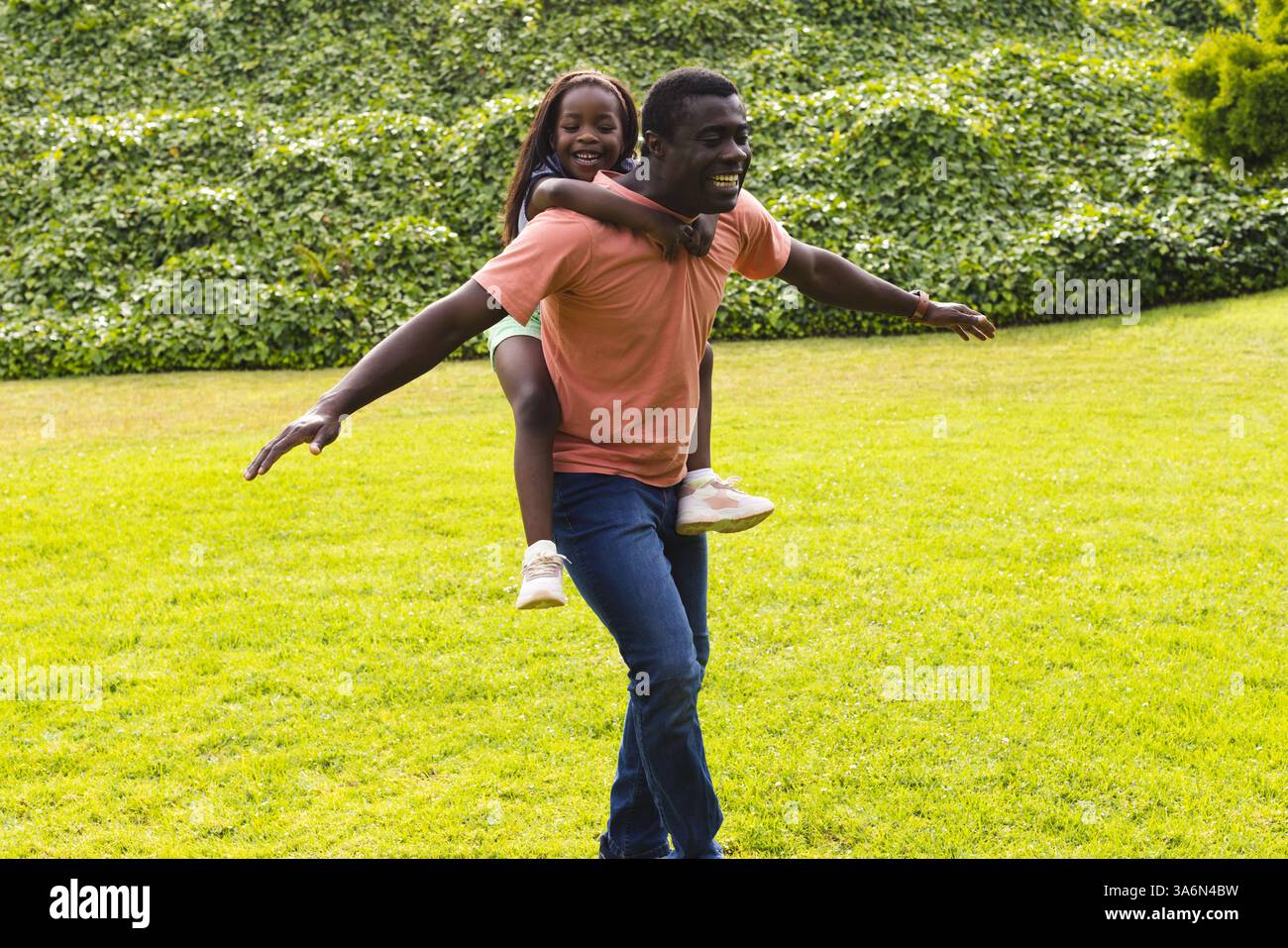 In park, African American father giving daughter piggyback ride, both ...