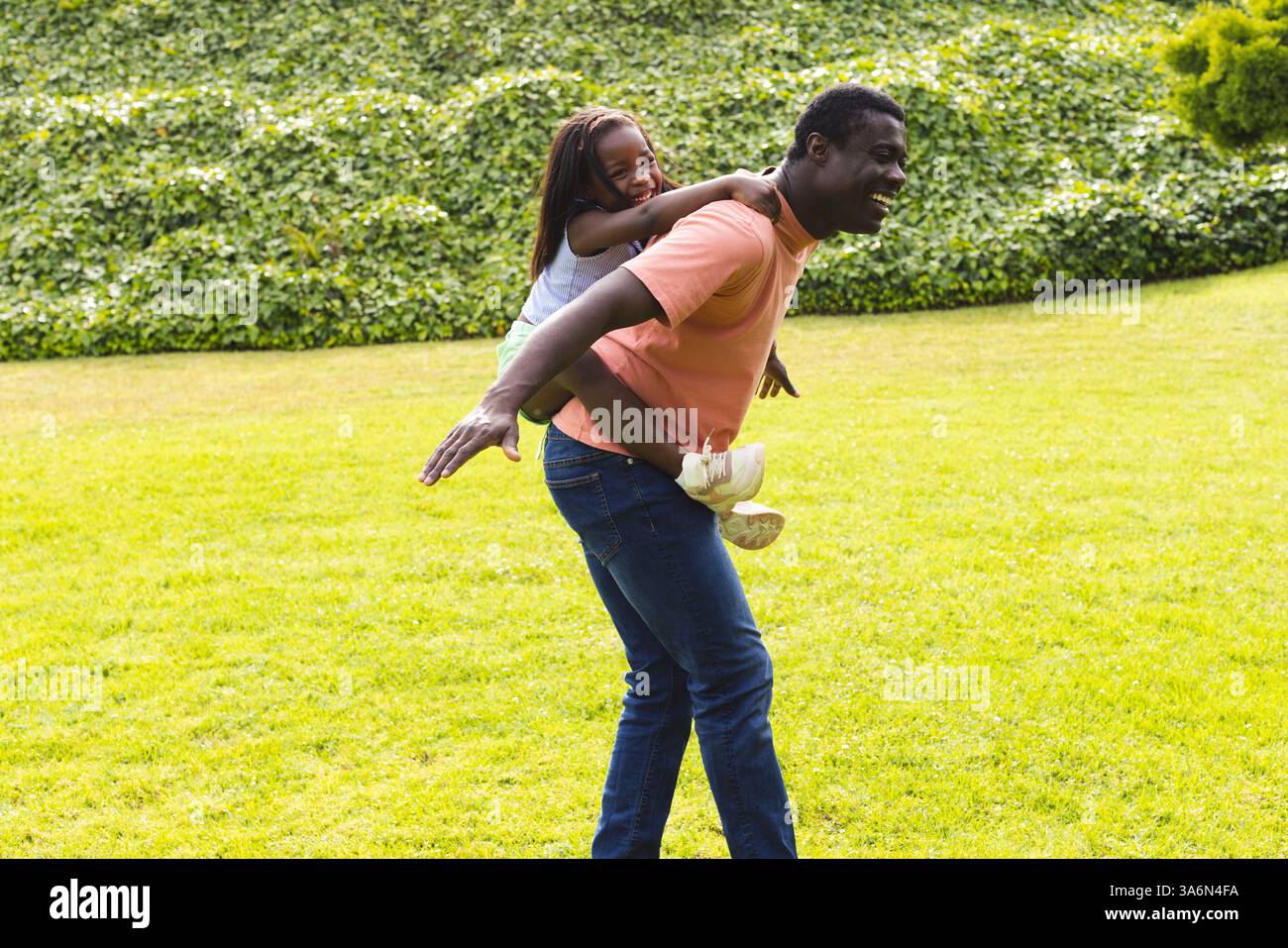 Father giving piggyback ride to daughter in park, both laughing ...