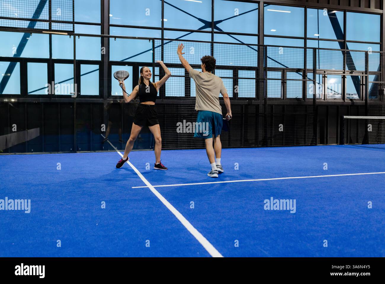 Celebrating victory, two players high-fiving on indoor padel tennis ...