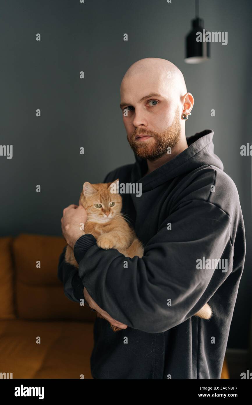 Vertical portrait of handsome bald man man hugging ginger cat looking ...