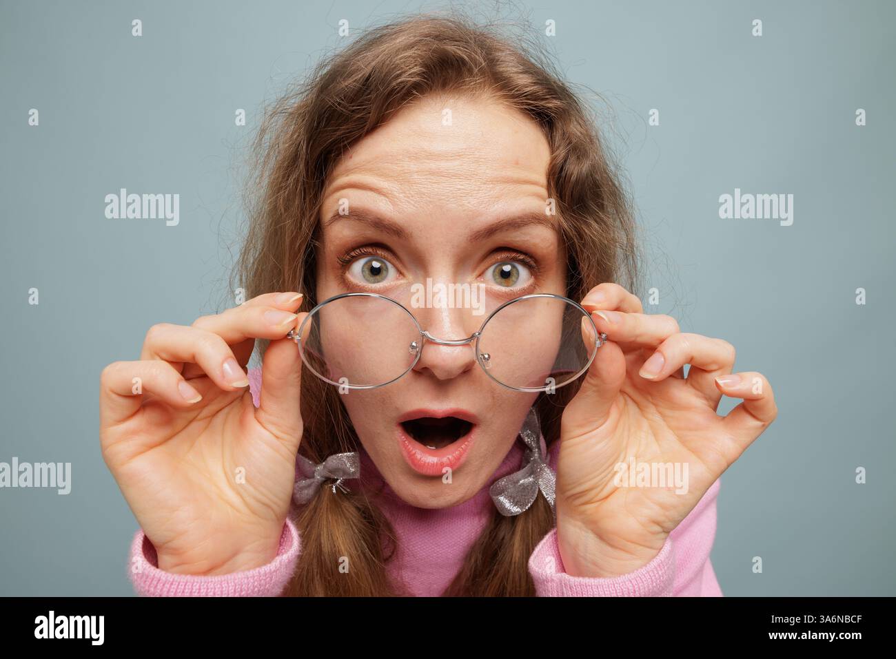Surprised young woman lifting round glasses in shock, eyes wide open ...