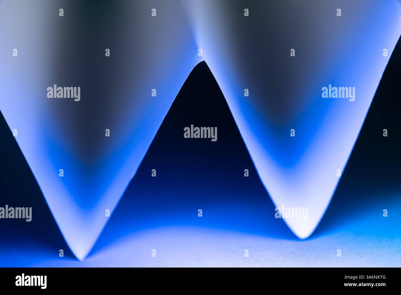 Curved sheets of paper form sharp peaks and valleys, illuminated by a ...