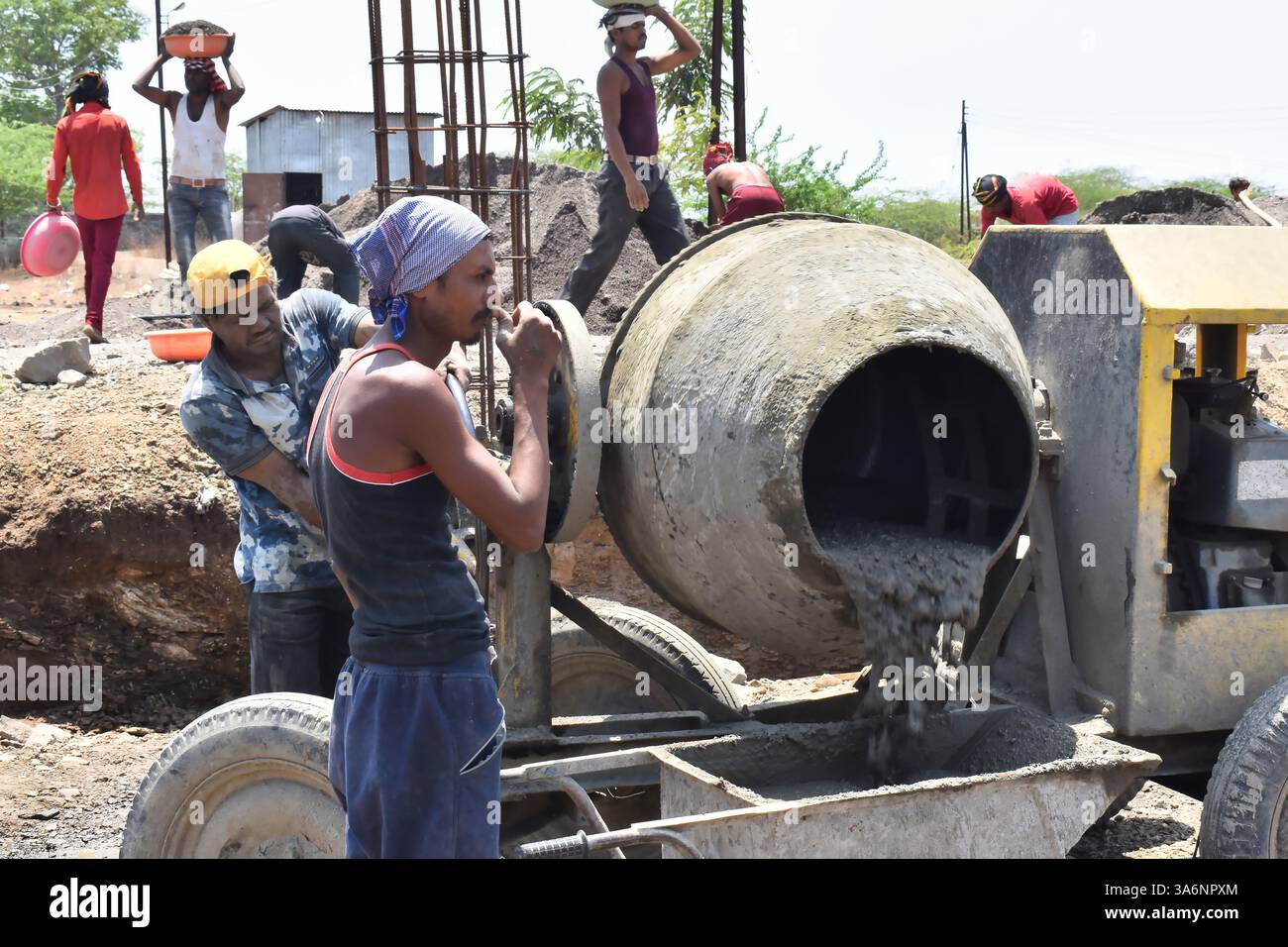 Construction workers operating a concrete mixer at a building site ...