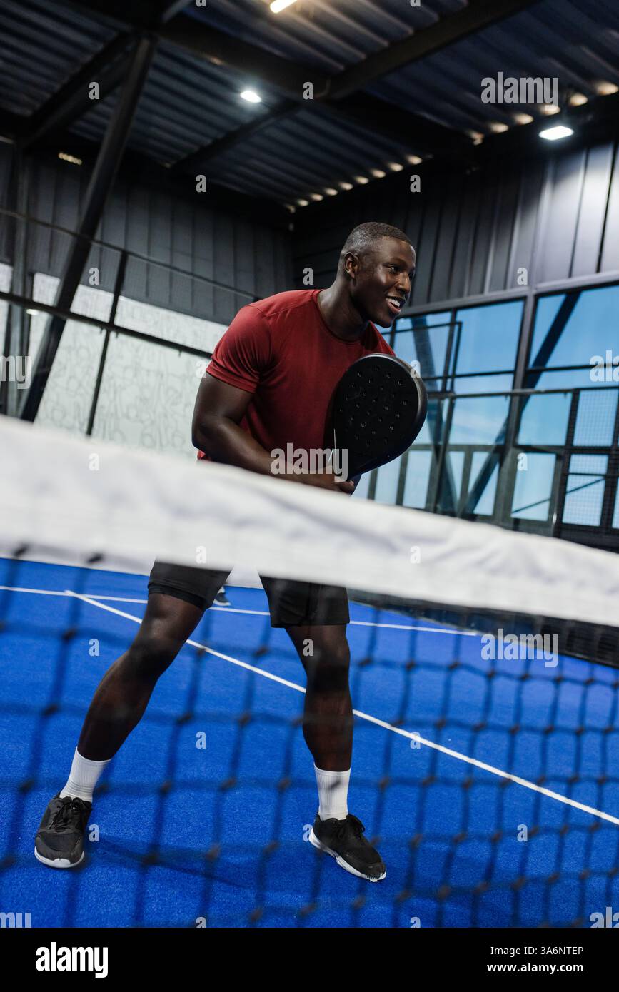 African American man playing padel tennis indoors, smiling and holding ...