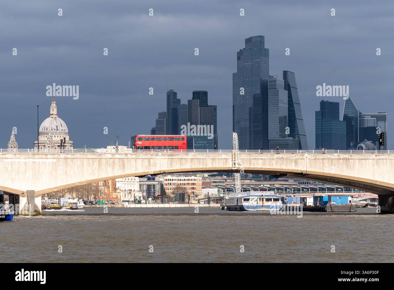 Red bus crossing Waterloo Bridge over the River Thames with the City of ...