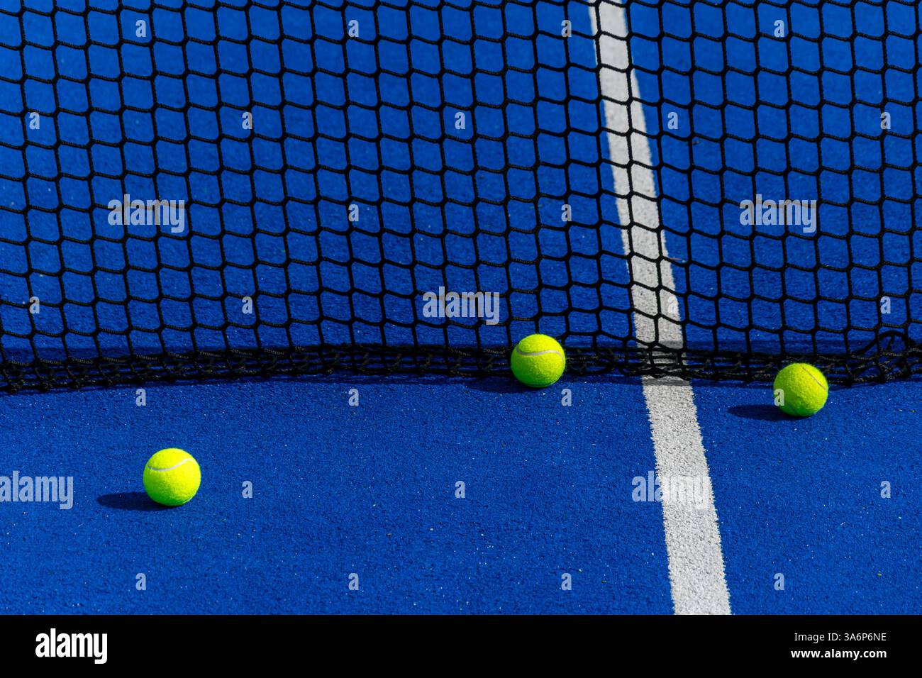 three padel balls near the net in a blue padel tennis court, racquet ...