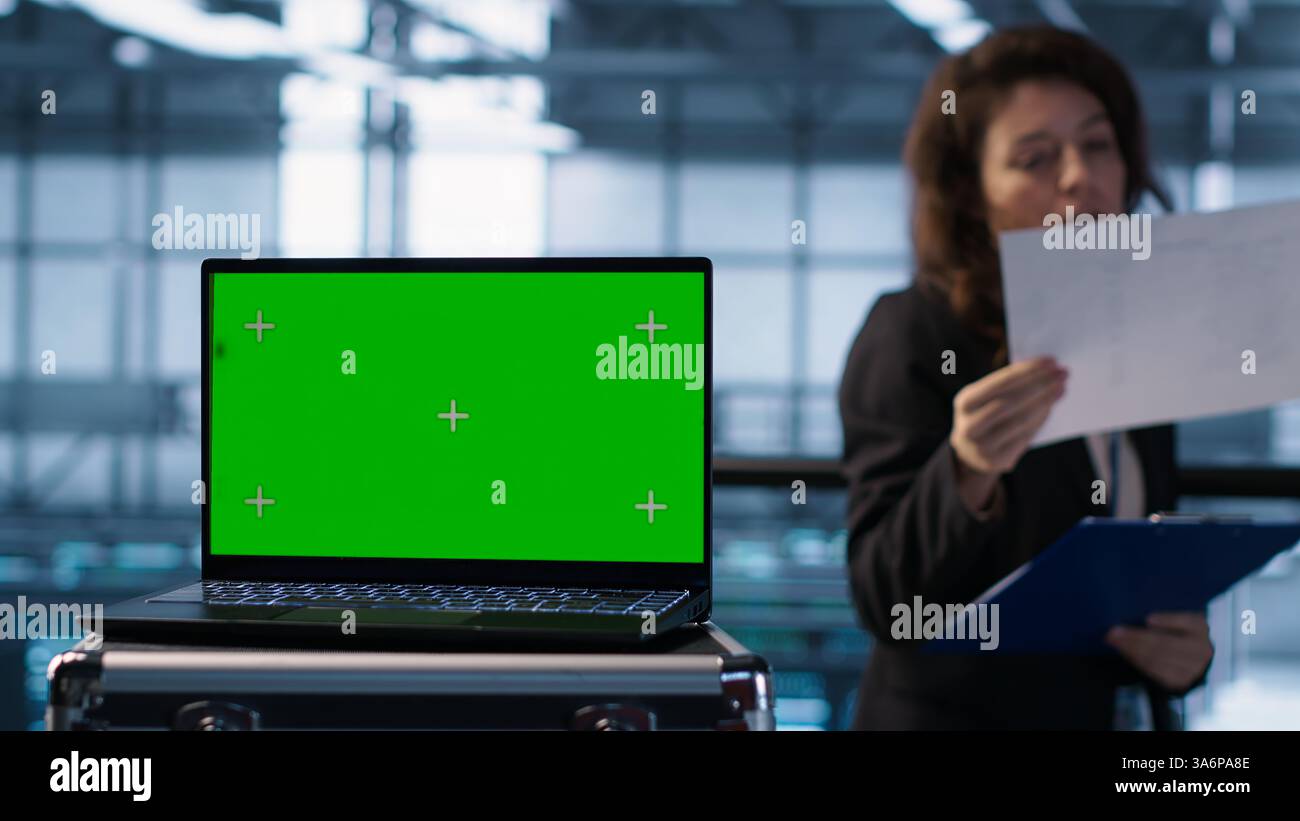 Green screen laptop used by data center admins in blurry background reviewing equipment ...