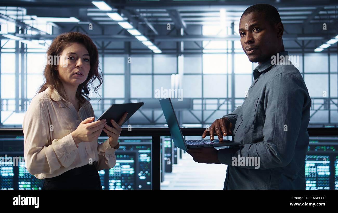 Data scientists in server room using laptop and tablet, executing security patches, verifying ...